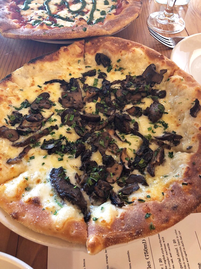 The wild mushroom pizza emerges from the wood-fired oven looking like a forest floor transformed into edible art. Fungi never tasted so divine.
