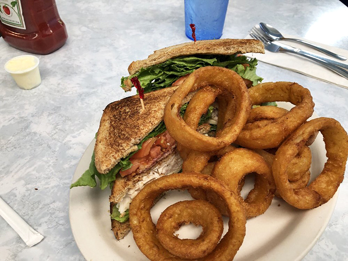 The club sandwich&mdash;mankind's greatest architectural achievement involving bread. Those golden onion rings aren't just sides, they're the supporting actors who steal the scene.