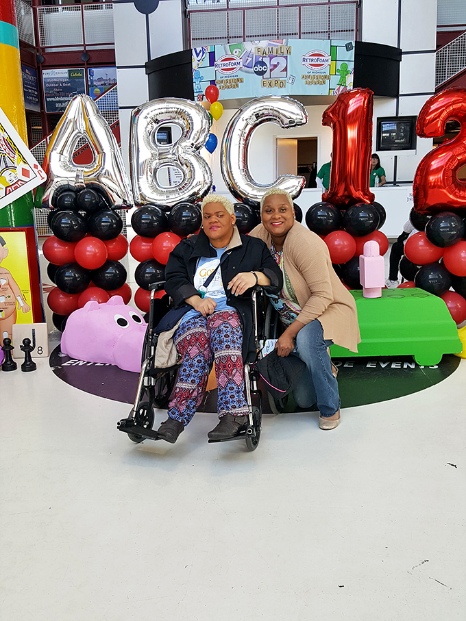 The image shows visitors enjoying a special event at the outlet mall, with decorative balloons creating a festive atmosphere for shoppers.