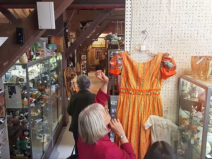 Vintage clothing enthusiasts examine a vibrant orange dress that probably witnessed more disco moves than John Travolta himself.