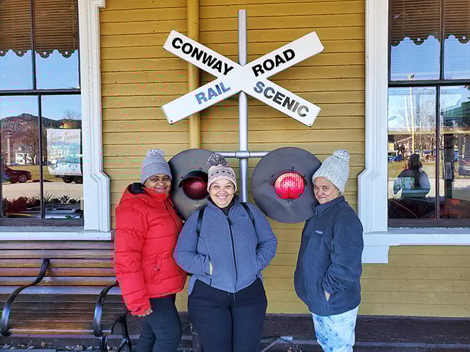 The universal language of train enthusiasm brings friends together at the Conway Scenic Railroad's iconic crossing sign—a perfect photo opportunity.