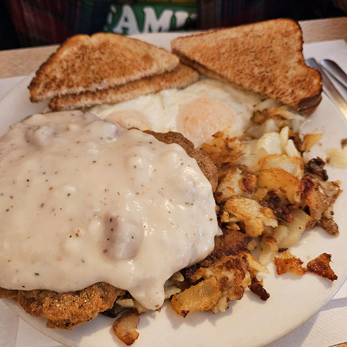 The legendary country fried steak, smothered in peppery gravy that cascades like a savory waterfall over crispy, seasoned breading. This is what dreams are made of.