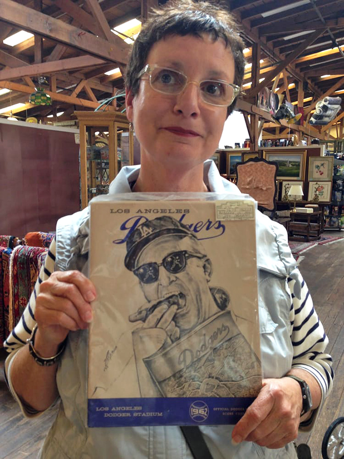 The image shows a visitor holding what appears to be vintage memorabilia in the spacious, beam-ceilinged interior of the antique mall.