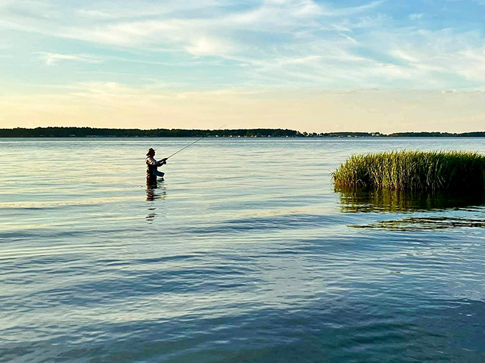 The patient angler stands in silent conversation with the water, practicing the art of fishing where time slows to match the gentle bay ripples.