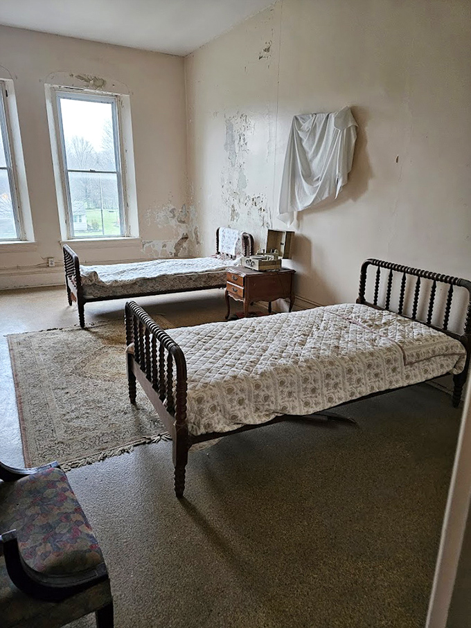 Twin iron beds await phantom occupants in this eerily preserved room, where peeling paint and worn floors tell stories of those long gone.