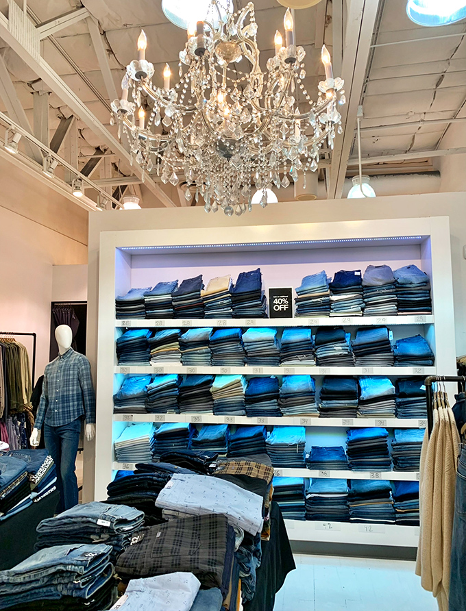 Beneath a crystal chandelier, denim stacks reach toward heaven like a shrine to casual fashion.