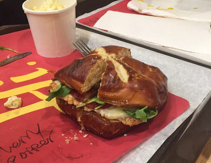 Not just any sandwich, but architectural brilliance on a pretzel bun. The layers of flavor here deserve their own blueprint.