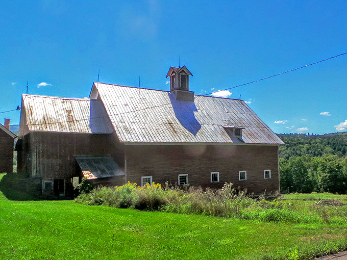 A bright red barn sits peacefully under clear blue skies in Waitsfield, surrounded by rolling hills and fresh green fields.