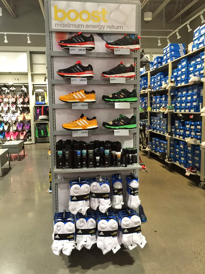 Adidas Boost sneakers lined up like soldiers ready for duty &ndash; protecting your feet and your budget simultaneously. The wall of blue boxes behind suggests reinforcements are ready.