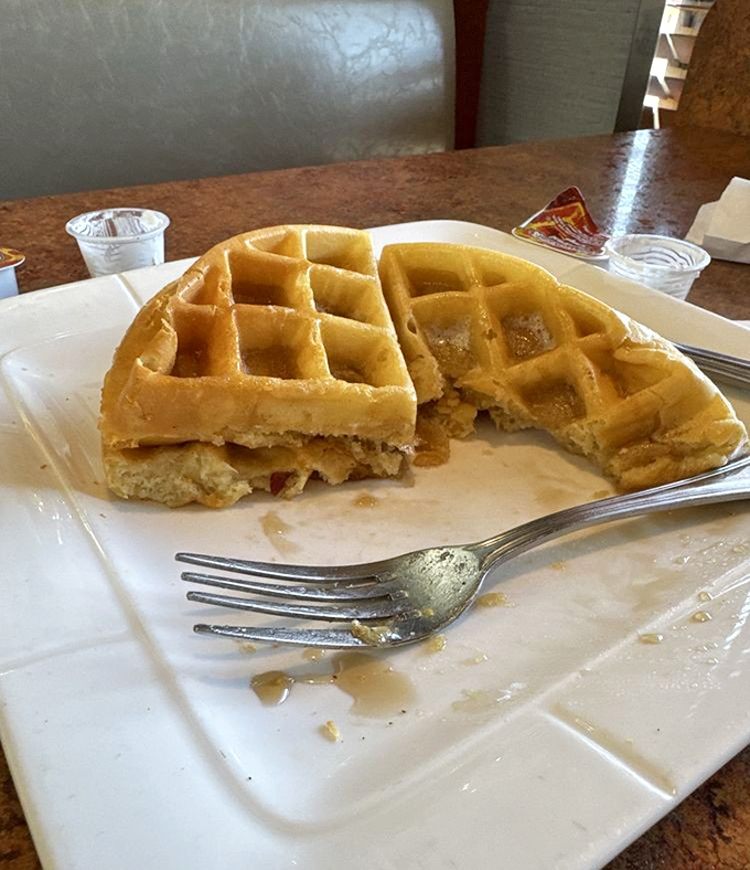 The Belgian waffle arrives golden and crisp, with deep pockets practically begging for maple syrup. Half-eaten because nobody has the willpower to photograph before diving in.