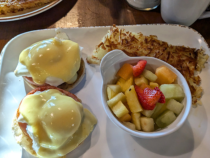 Eggs Benedict sitting pretty with hollandaise cascading down, plus hash browns and fresh fruit because balance matters, even at breakfast.