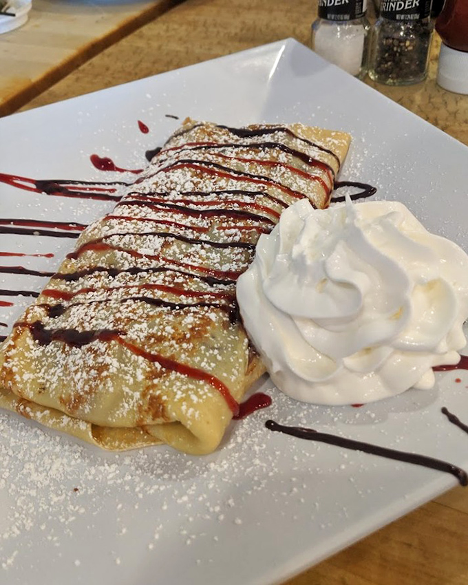 A crepe dressed for success with powdered sugar, artful drizzles, and a dollop of whipped cream that's basically wearing a tuxedo to breakfast.