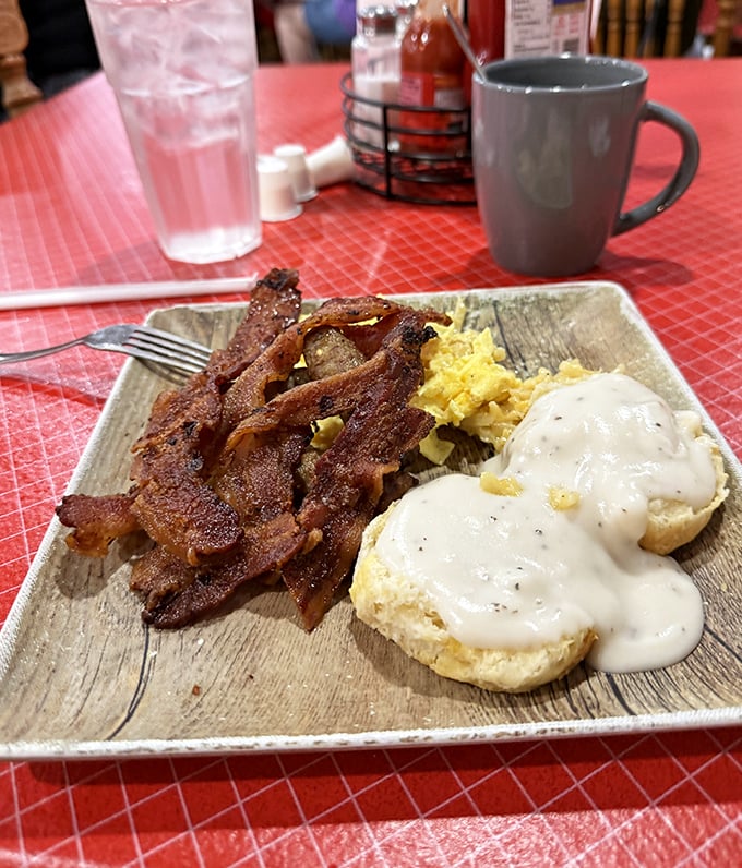 The holy trinity of Southern breakfast: crispy bacon, fluffy eggs, and biscuits smothered in gravy that could make a cardiologist weep with both concern and envy.