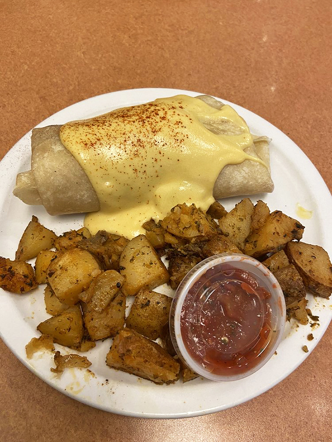 Breakfast burrito baptized in hollandaise – a tortilla-wrapped treasure chest with crispy potatoes standing guard alongside.
