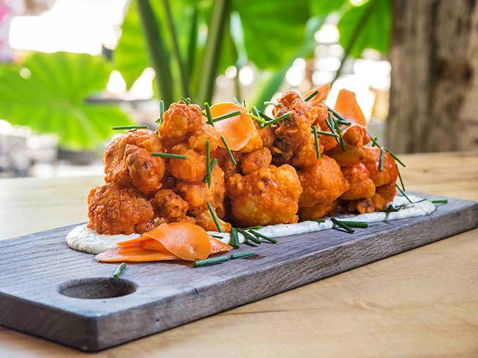 Buffalo cauliflower that makes vegetarians feel smug and carnivores question their life choices&mdash;crispy, saucy perfection on a wooden board.