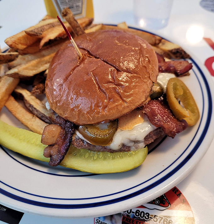 Not just any burger &ndash; this masterpiece stacks bacon, cheese, and pickles between a toasted bun with fries standing guard alongside.