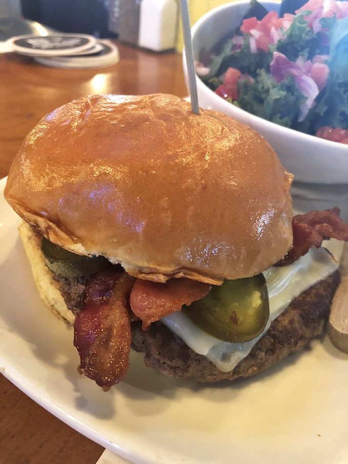 A burger that requires both hands and a strategy &ndash; notice how the perfectly toasted bun contains a masterpiece of beef, bacon, and pickles waiting to be devoured.