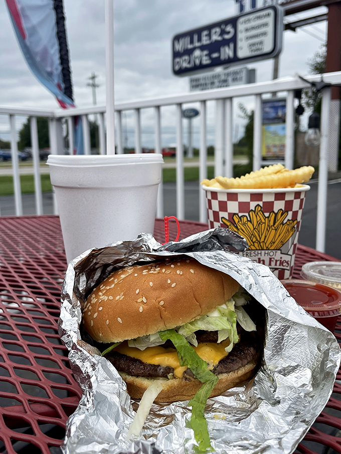 The cheeseburger in its natural habitat: wrapped in foil, nestled beside crispy fries, waiting to fulfill its destiny on a red metal table.