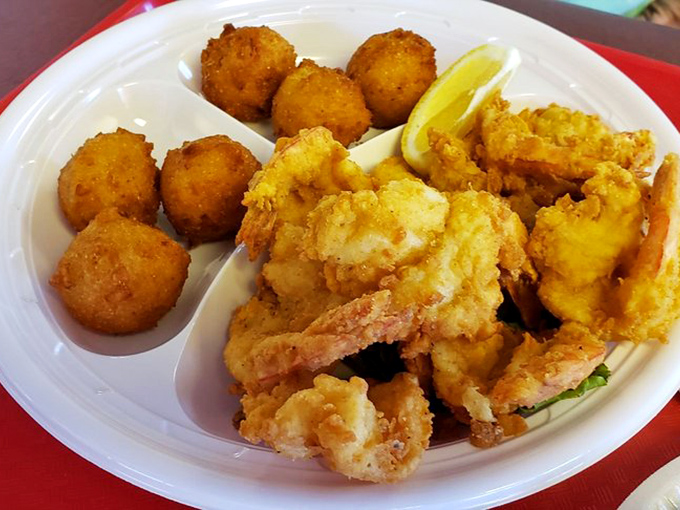 A plate of golden, crispy butterfly shrimp is served with hush puppies and lemon wedges for a delicious seafood meal.