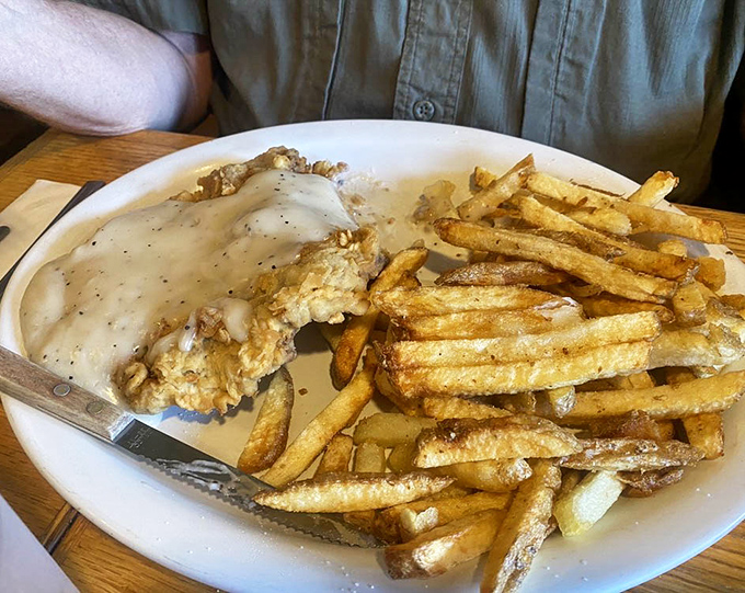 Country gravy cascading over chicken fried steak like a delicious waterfall, with fries standing by for the inevitable "just one more bite" moment.