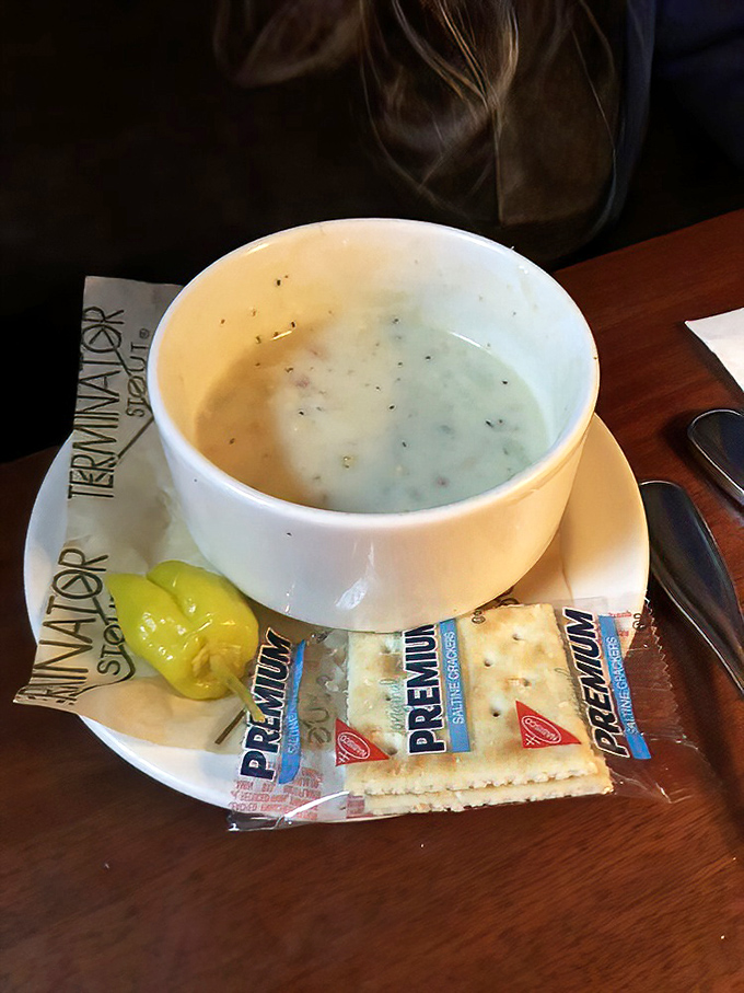 A bowl of creamy clam chowder with oyster crackers and a pickle spear. New England tradition meets Pacific Northwest hospitality in every spoonful.