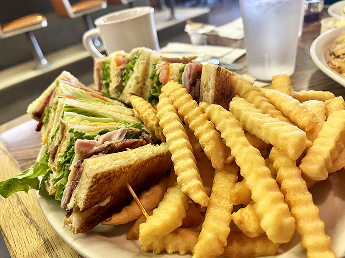 The club sandwich&mdash;architecture you can eat. Layers of satisfaction held together by toothpicks and tradition, with a side of crinkle-cut fries that demand to be savored one by one.