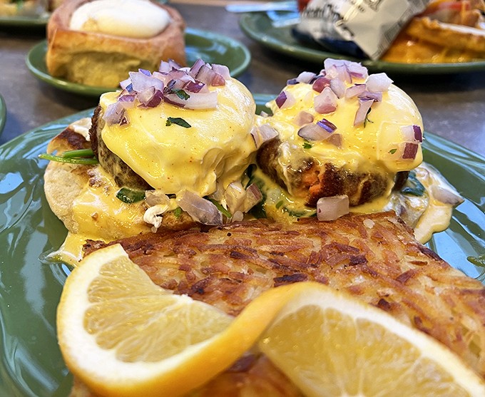 Benedict perfection: Two golden-crowned English muffins topped with what appears to be salmon cakes, hollandaise, and a sprinkle of red onion. Breakfast royalty.