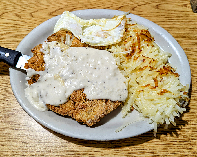 Country fried steak wearing its gravy coat with pride, while hash browns stand at attention nearby &ndash; a breakfast alliance that's never let anyone down.