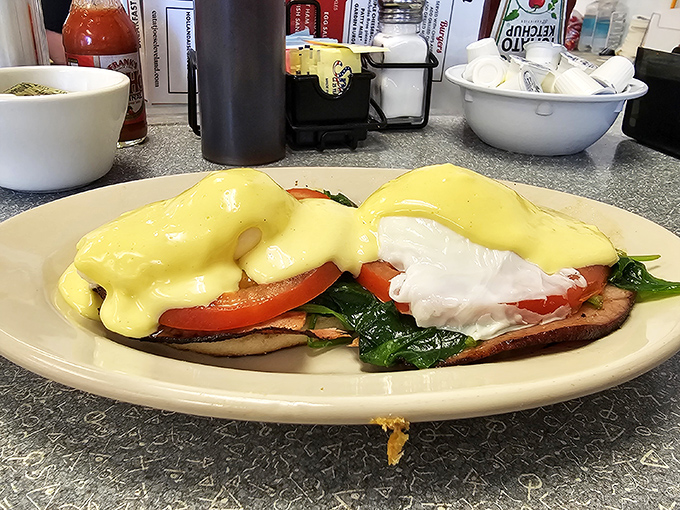 Eggs Benedict done right—creamy hollandaise cascading over perfectly poached eggs and fresh tomato. Breakfast architecture at its finest.