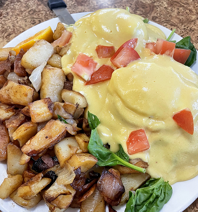 Eggs Benedict draped in hollandaise sauce so luxurious it deserves its own theme song, served alongside perfectly seasoned potatoes that understand their assignment.
