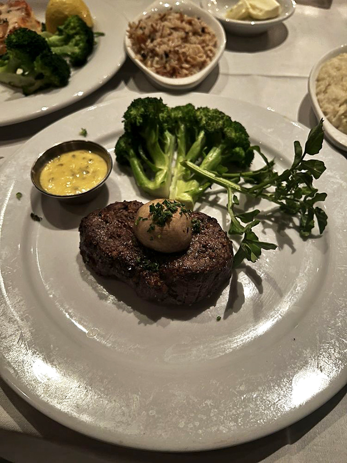 A filet mignon topped with compound butter that melts like your resolve when the dessert menu arrives. The hollandaise sauce stands by, ready for its moment.