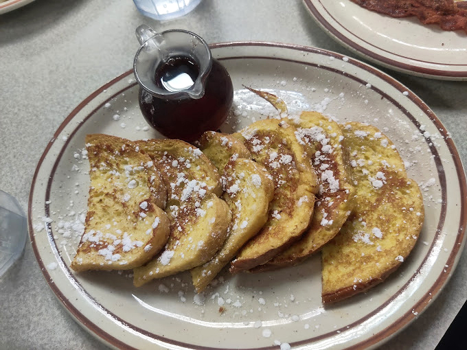 French toast dusted with powdered sugar like the first perfect snowfall of winter. That little pitcher of syrup is about to make magic happen.