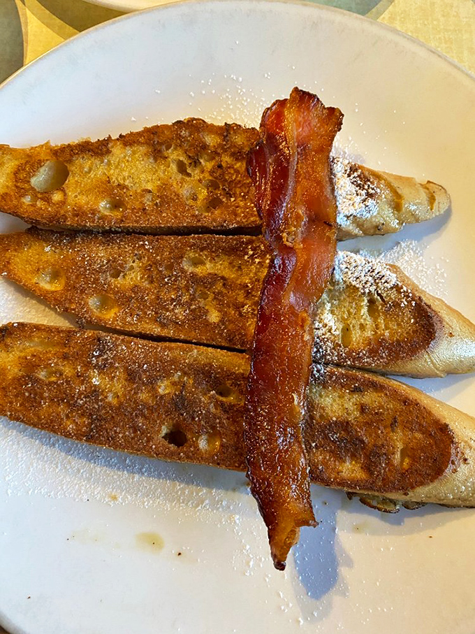 French toast fingers arranged like edible art, dusted with powdered sugar and crowned with a strip of bacon that's achieved crispy-chewy perfection.