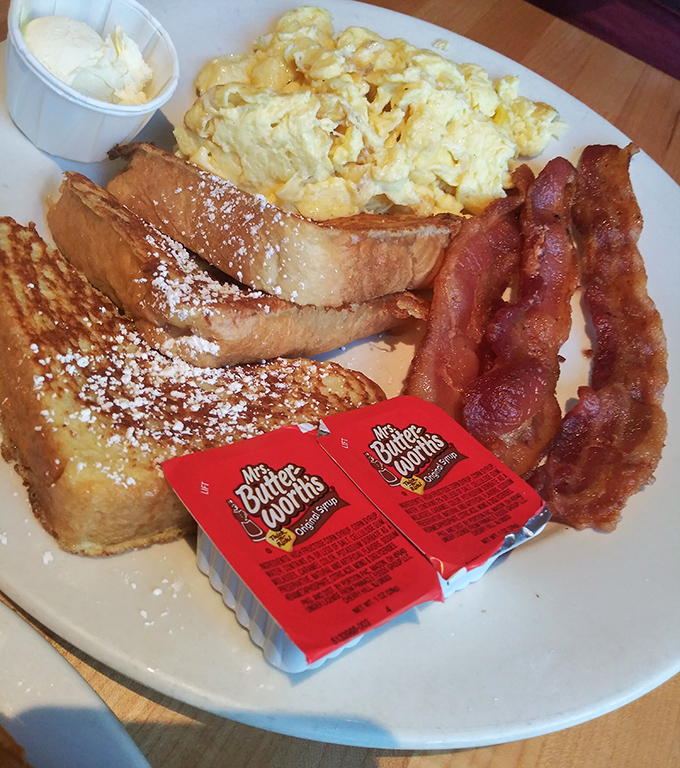 Breakfast perfection on a plate: golden French toast dusted with powdered sugar, fluffy scrambled eggs, and bacon cooked to that magical point between chewy and crisp.