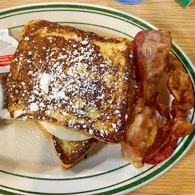 French toast dusted with powdered sugar alongside crispy bacon represents breakfast perfection on a single plate of happiness.