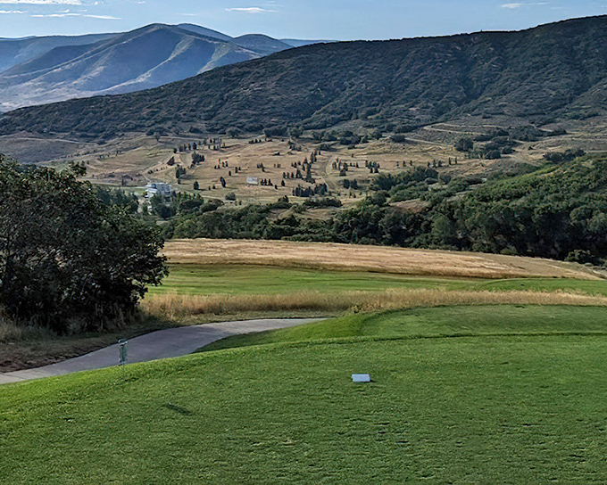 The golf course unfolds like a green carpet rolled out for visitors, with mountains standing guard like nature's own gallery of spectators.