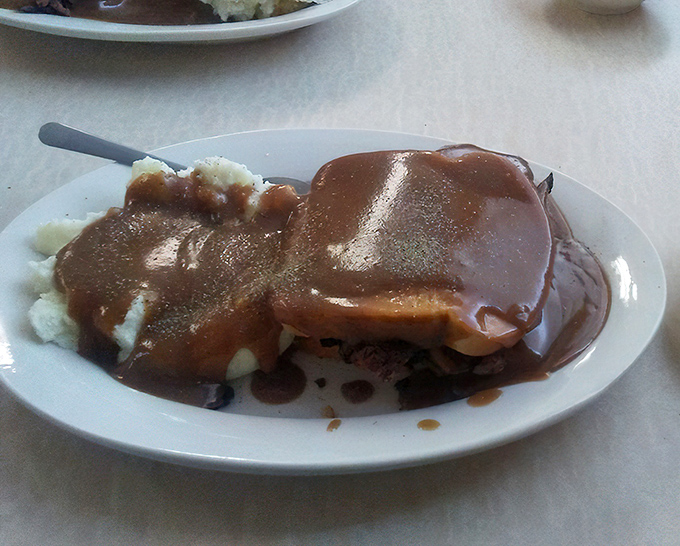 This hot beef sandwich doesn't just sit on the plate – it lounges in gravy like it's taking a delicious spa day.