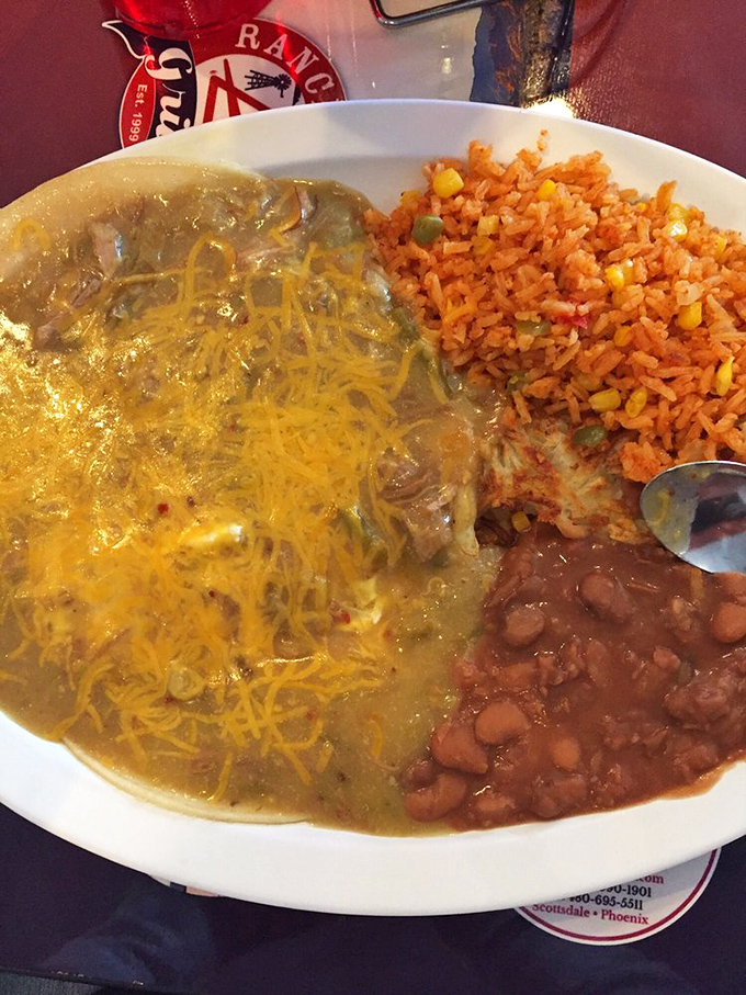 Mexican breakfast magic: green chile sauce blankets this dish like a warm Arizona sunrise, with Spanish rice and beans playing delicious supporting roles.
