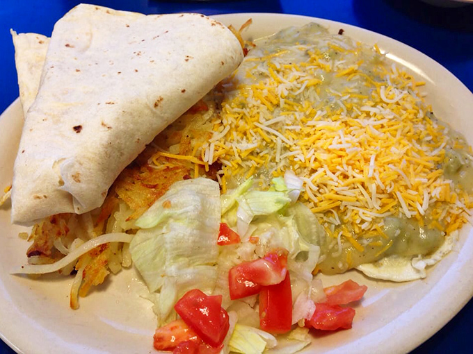Huevos Rancheros done right means eggs, cheese, crispy hash browns, and that essential New Mexico green chile situation happening.