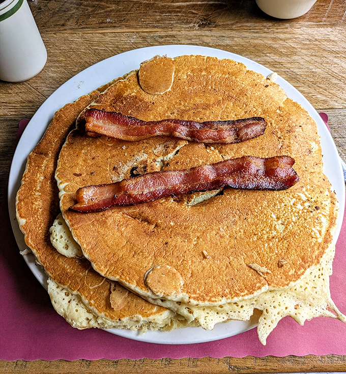 Pancakes so magnificent they deserve their own ZIP code. Those bacon strips aren't garnish&mdash;they're the VIP guests at this carb carnival.