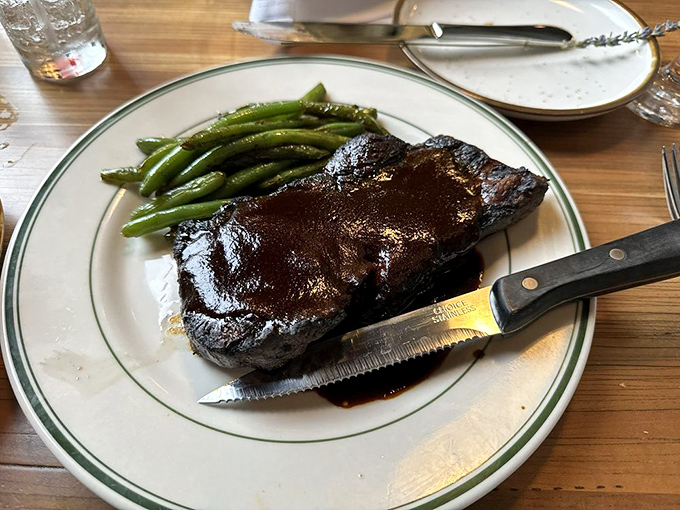 A New York strip steak glistening with promise, flanked by vibrant green beans&mdash;proof that sometimes the simplest preparations yield the most profound satisfaction.