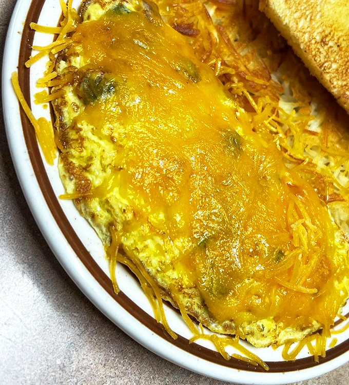 This omelet has more cheese pull than a romantic movie scene. The golden exterior hides treasures within, flanked by perfectly browned toast.