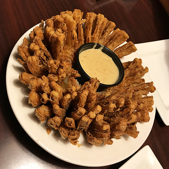 Onion straws arranged like a golden crown, with dipping sauce holding court in the center. Crispy, crunchy therapy that makes sharing feel like a moral dilemma.