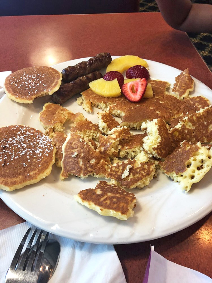 Pancake artistry meets sausage diplomacy on a plate where fruit adds color commentary to this breakfast symphony.