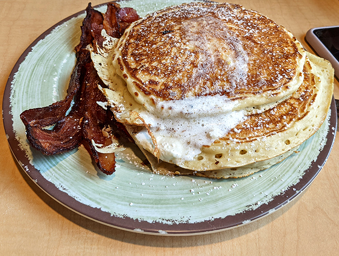 Pancake perfection achieved: golden-brown discs stacked higher than your morning expectations, with bacon standing by for moral support.