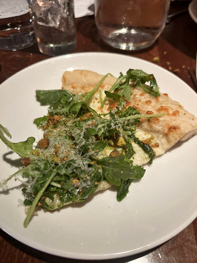 This isn’t just pistachio pizza—it’s a garden party on a crust, where arugula and what appears to be pesto create a vibrant celebration of green goodness.