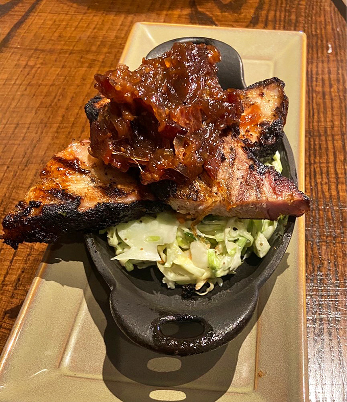 Pork belly perched atop fresh slaw &ndash; a study in contrasts where smoky richness meets crisp vegetables in perfect harmony.