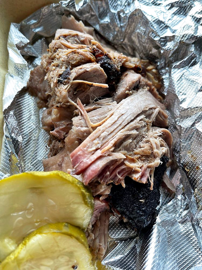 Pulled pork so tender it practically surrenders at the sight of your fork, accompanied by pickle slices that cut through the richness like a citrus ninja.