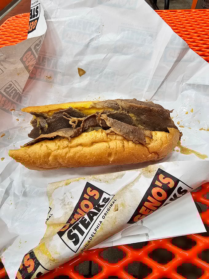 A cheesesteak in its natural habitat&mdash;wrapped in paper, resting on an orange table. The "Philly lean" eating position was invented for precisely this moment.