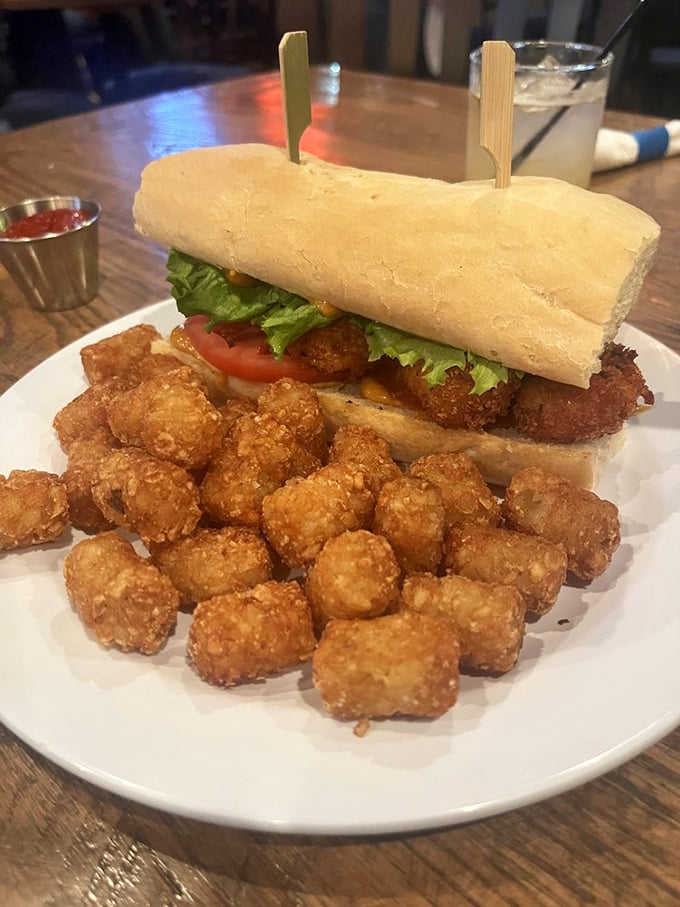 A sandwich that demands two hands and your full attention, accompanied by golden tater tots that crunch like childhood memories.
